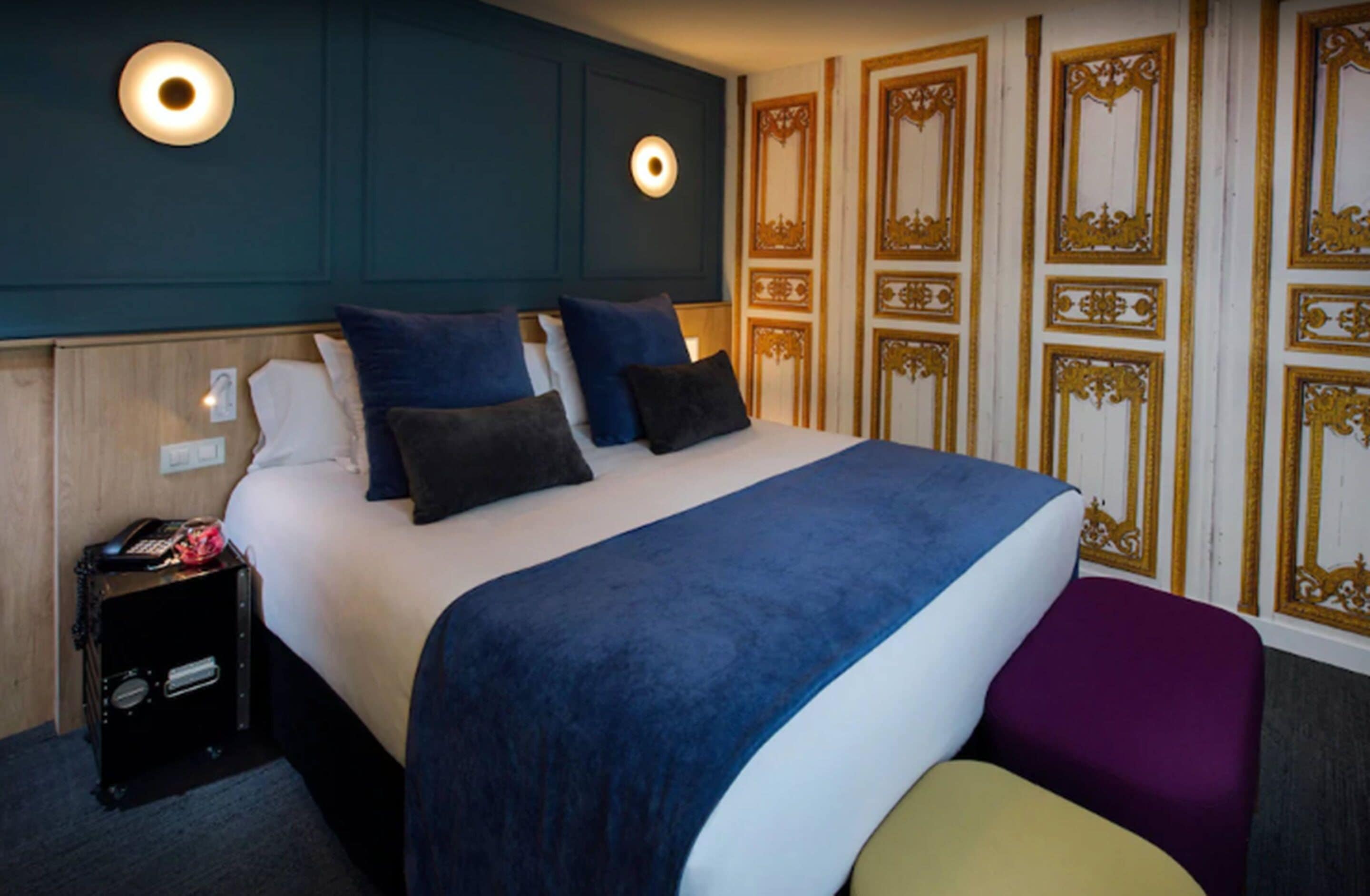 Quarto de hotel com uma cama grande, duas luminárias de cabeceira, uma mesa de cabeceira com telefone e um painel decorativo na parede.