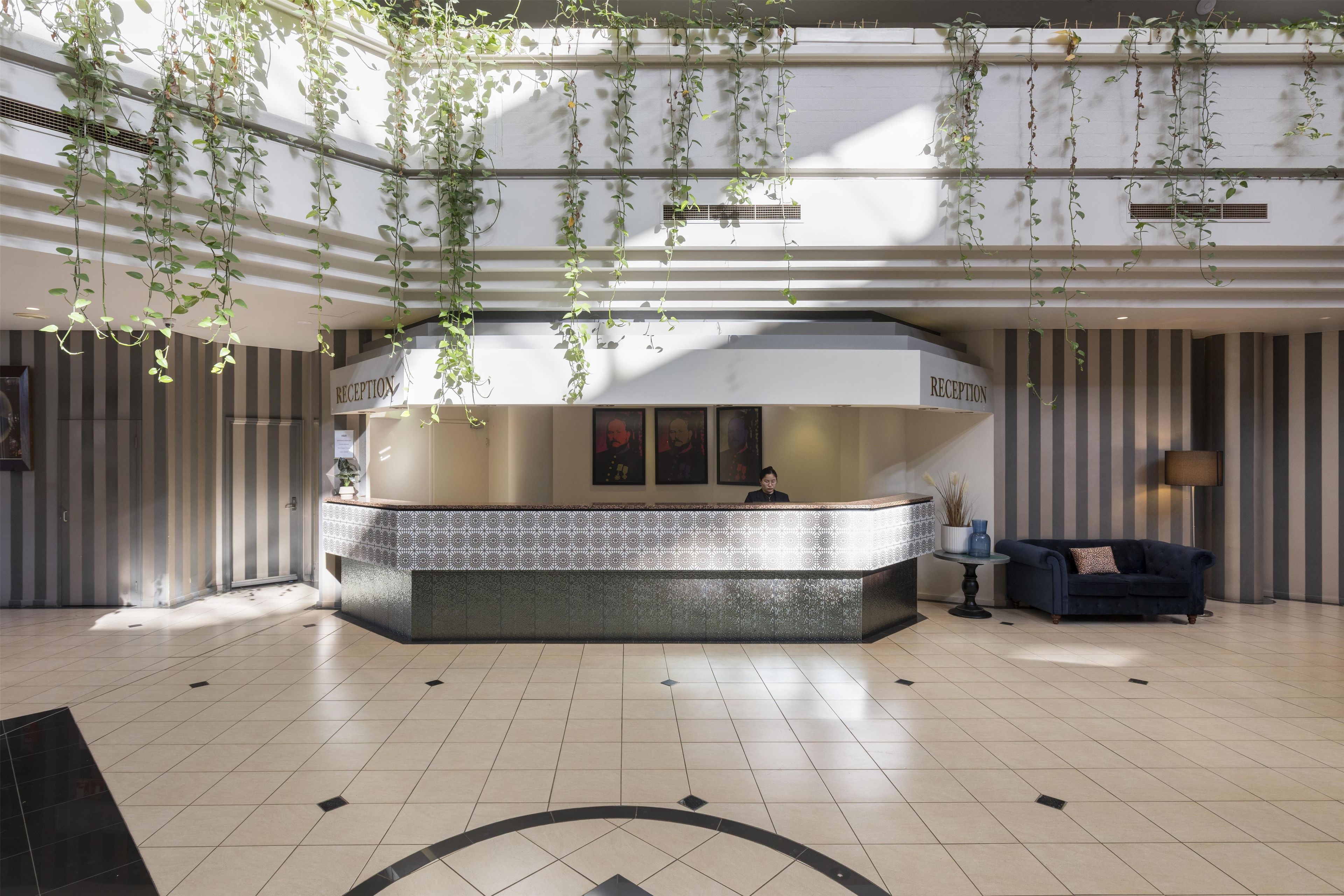 Uma área de recepção com piso de azulejos, balcão de atendimento, um sofá e plantas penduradas.