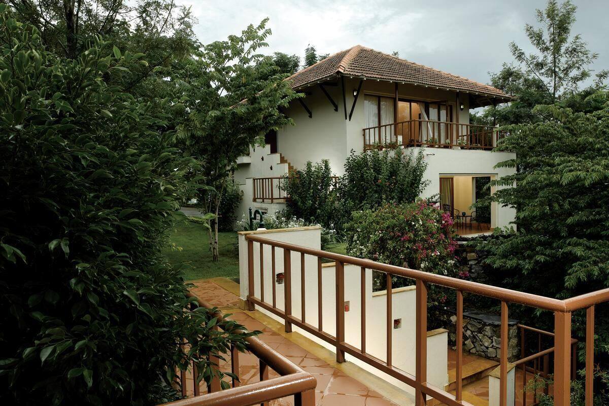 Uma casa de dois andares com varanda, rodeada por vegetação exuberante.