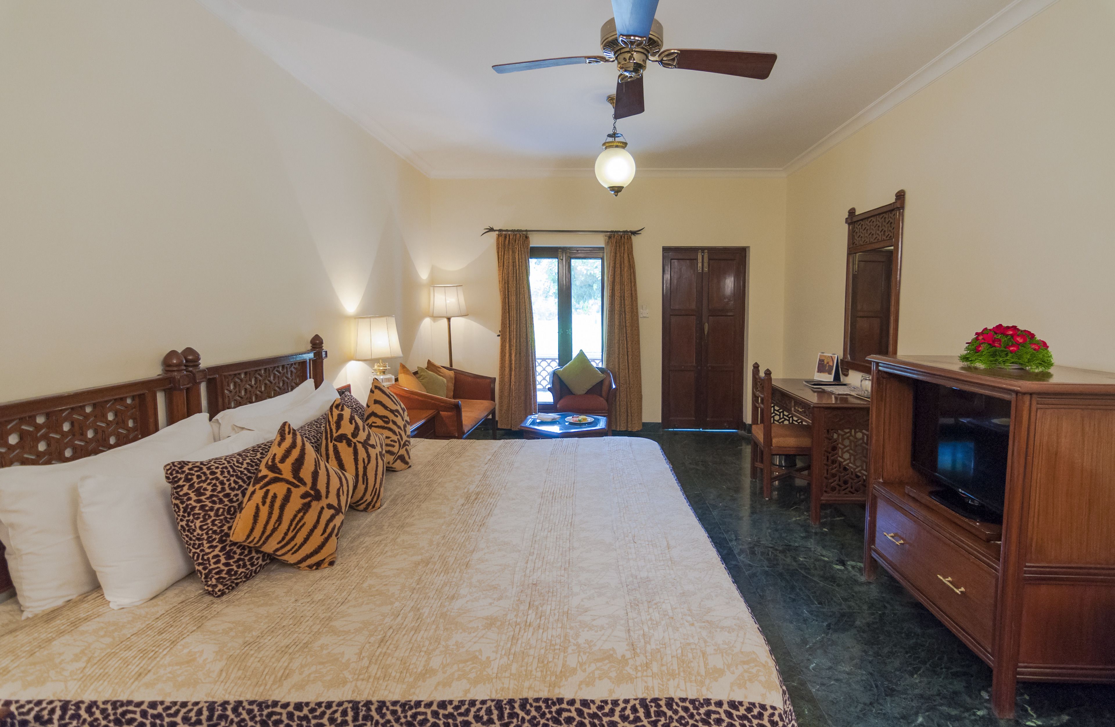 Quarto de hotel com uma cama grande, um ventilador de teto, uma televisão e uma escrivaninha com uma cadeira.