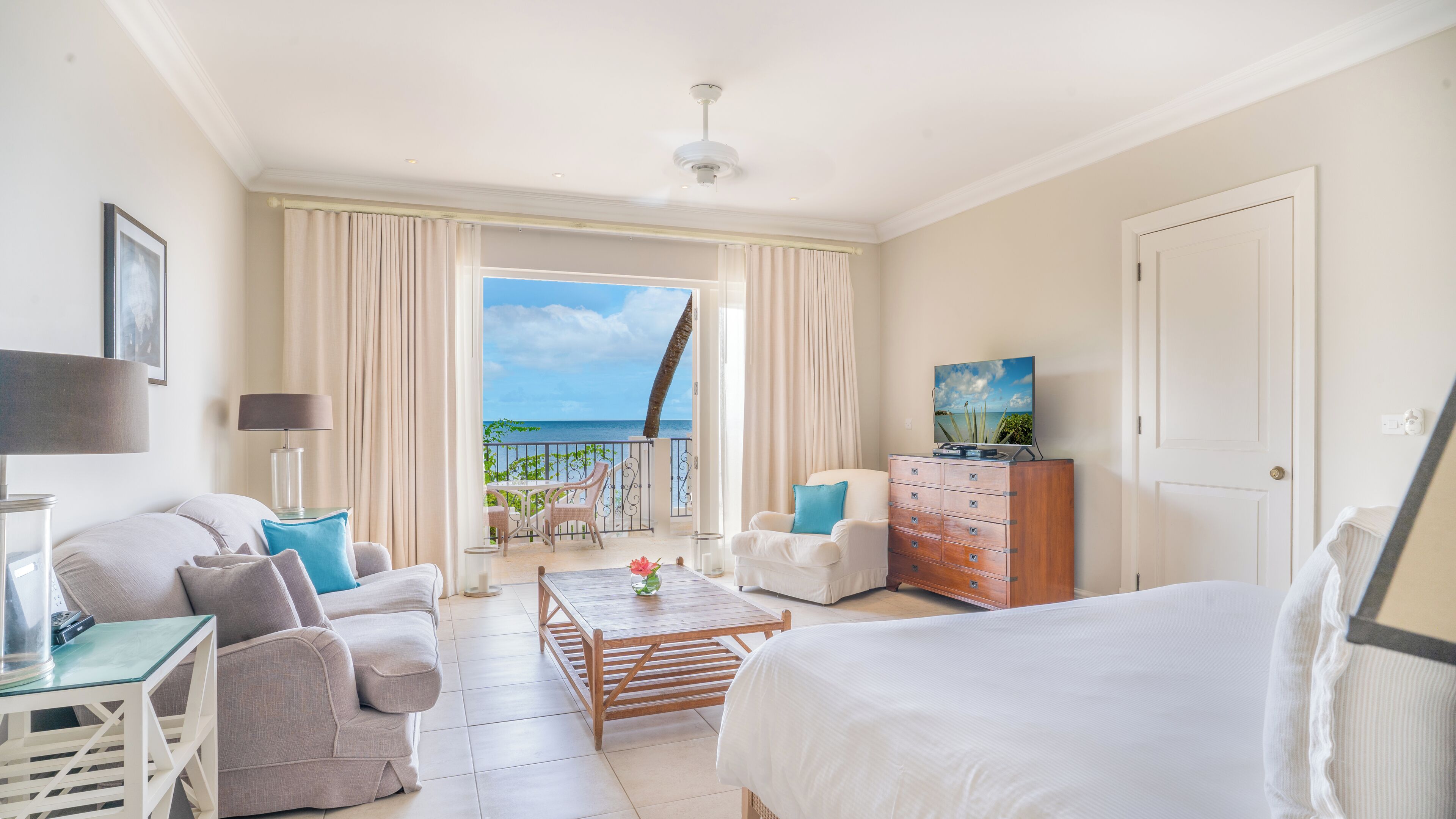 Quarto de hotel com varanda, uma cama, um sofá, mesa de centro e televisão.