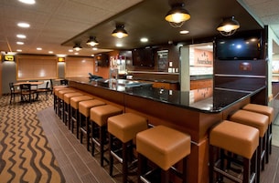 Uma área de bar com um balcão comprido, vários bancos e iluminação pendente.