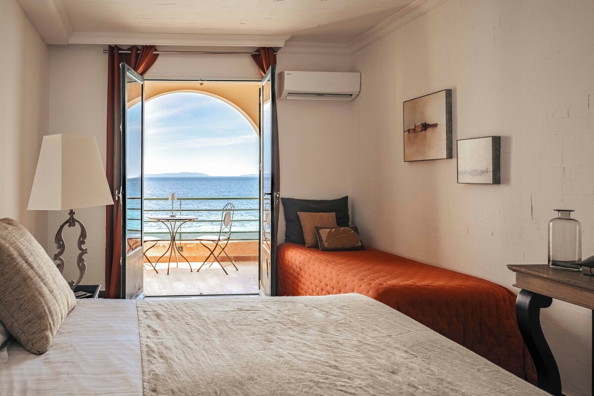 Quarto de hotel com cama, secretária, cadeira e vista para o mar.