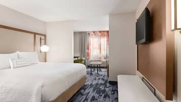 Quarto de hotel com cama grande, escrivaninha, cadeira, televisão na parede e janela com cortinas.