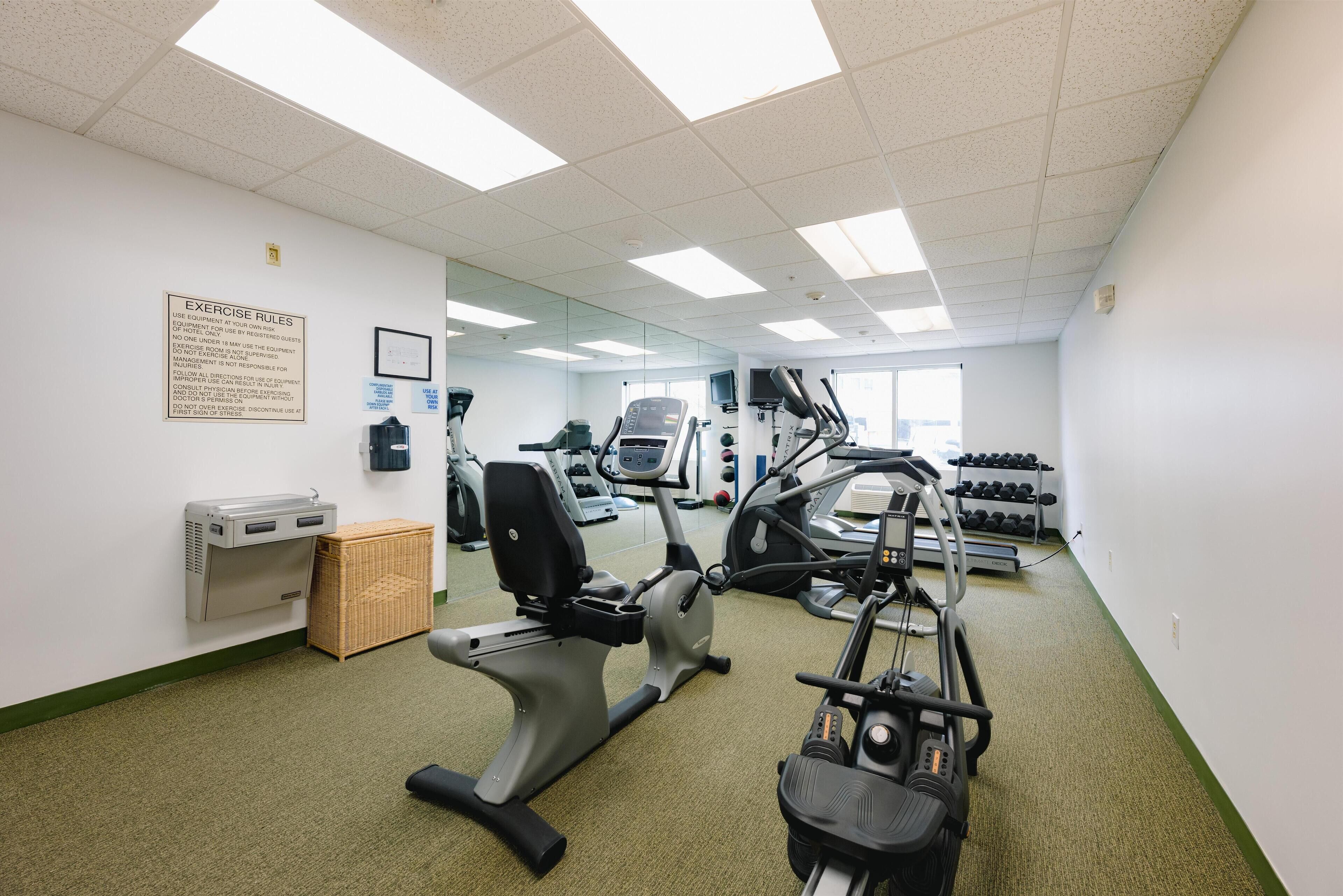Uma academia com máquinas de exercício, um espelho e um mural com as regras.