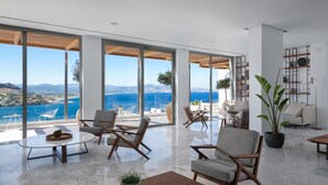 Uma sala de estar espaçosa com grandes janelas, vista para o mar e móveis modernos.