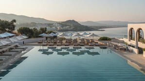 Área à beira da piscina com espreguiçadeiras e guarda-sóis, com vista para um corpo d'água e colinas ao longe.