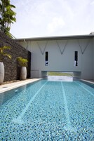 Uma piscina com água azul cristalina, rodeada por um muro de pedra e palmeiras.