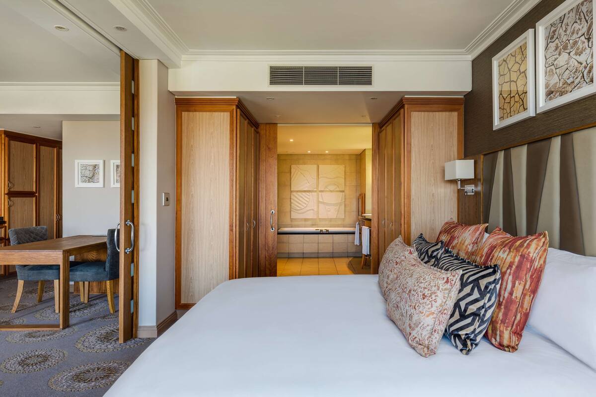 Quarto de hotel com uma cama grande, uma escrivaninha e um banheiro visível através de uma porta aberta.