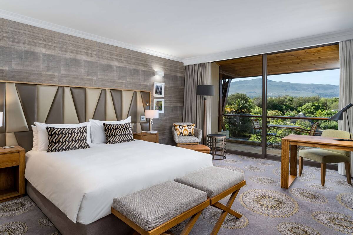 Quarto de hotel com cama grande, escrivaninha, cadeira e vista para o exterior.