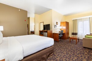 Quarto de hotel com uma cama grande, uma escrivaninha com computador, televisão e sofá.