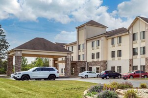Um hotel com vários andares, área de estacionamento coberta, vários veículos estacionados e um jardim ajardinado em primeiro plano.