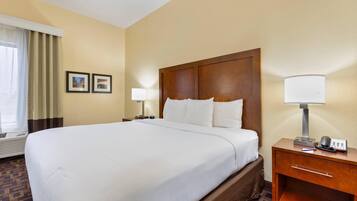 Quarto de hotel com uma cama grande, uma mesa de cabeceira com abajur, um criado-mudo e duas fotografias emolduradas na parede.