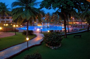 Área de piscina com palmeiras, um gazebo e cadeiras de descanso.