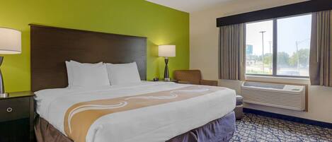 Quarto de hotel com uma cama grande, duas luminárias de cabeceira, uma janela com cortinas e um ar condicionado fixado na parede.