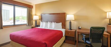 Quarto de hotel com uma cama grande, duas mesas de cabeceira com luminárias, uma escrivaninha com cadeira e uma janela com cortinas.