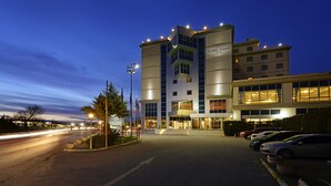 Um hotel de vários andares com design moderno, destacando uma entrada imponente e um estacionamento com diversos carros.