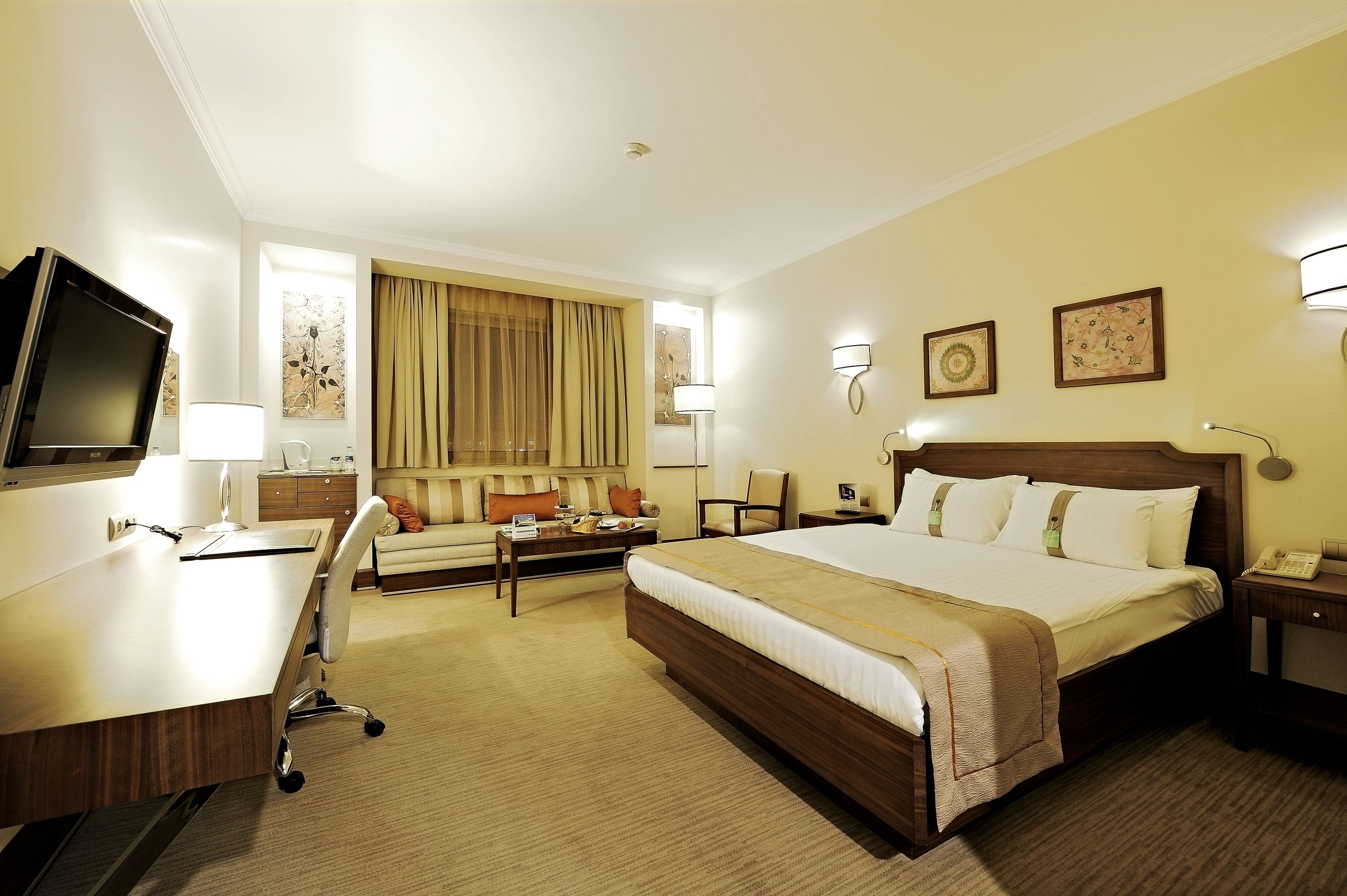 Quarto de hotel com uma cama grande, uma escrivaninha, uma cadeira, um sofá e uma televisão.