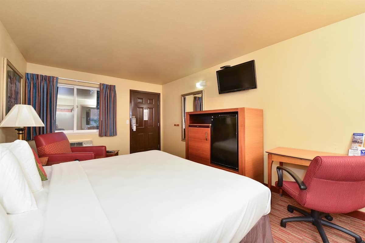 Quarto de hotel com cama, escrivaninha, televisão, frigorífico e janela com cortinas.