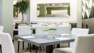 Uma área de refeições moderna com uma mesa retangular, cadeiras brancas e uma planta em vaso central.