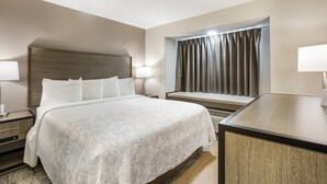 Quarto de hotel com cama grande, abajures, janela com cortinas e escrivaninha com luminária.