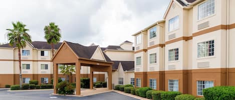 Um hotel com vários andares, entrada coberta, palmeiras e um gramado bem cuidado.