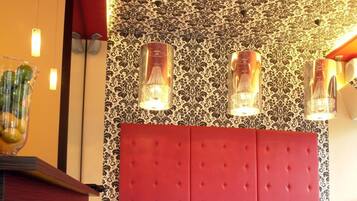 Uma área de bar moderna com assentos estofados em vermelho, banquetas de metal cromado e iluminação pendente.