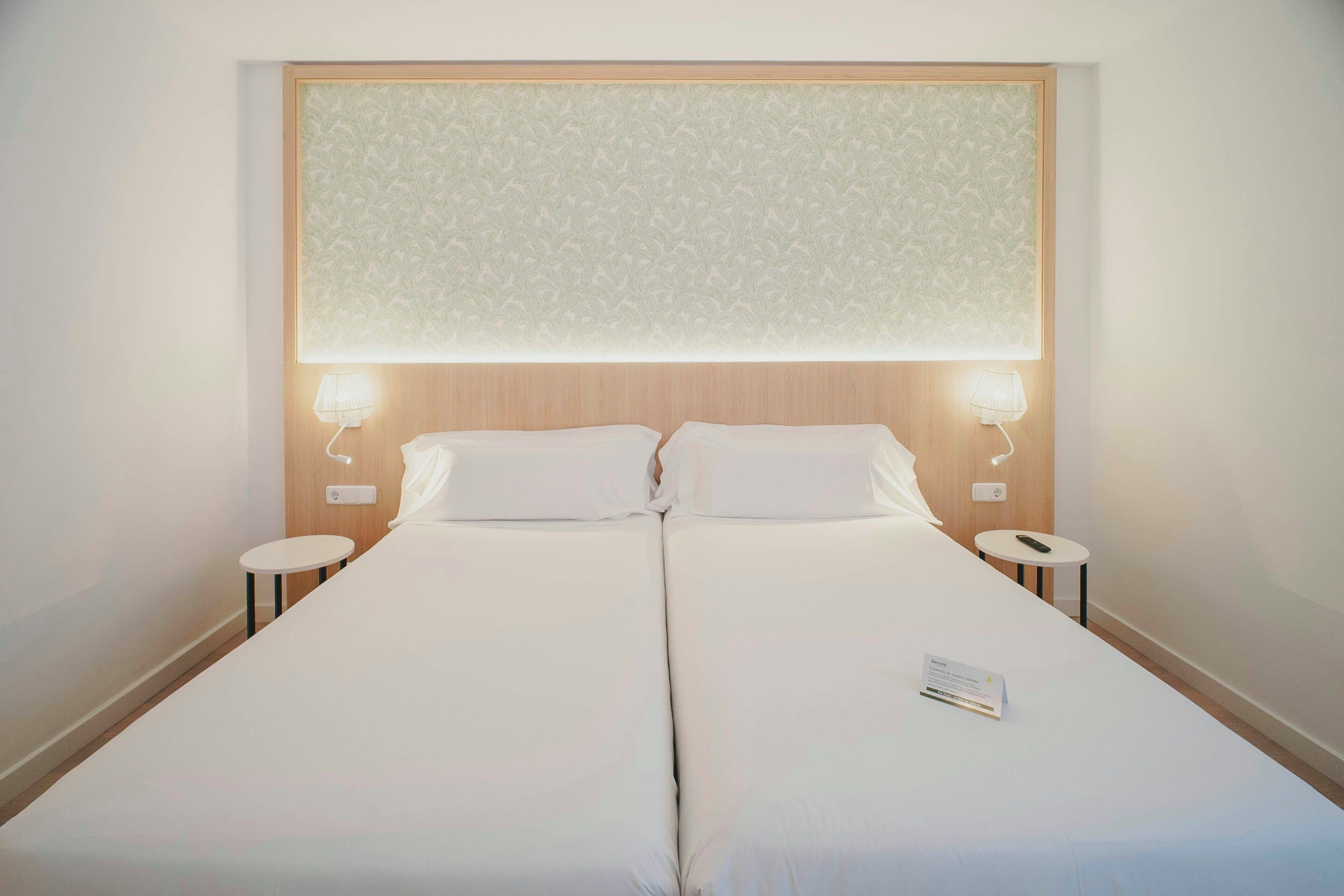 Uma cama de casal com cabeceira, duas mesas de cabeceira com luminárias e uma pequena mesa redonda.
