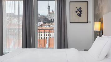 Quarto de hotel com uma cama grande, vista para a cidade, uma obra de arte emoldurada e um abajur.