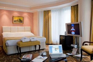Quarto de hotel com uma cama, uma escrivaninha com um laptop, uma televisão e um quadro na parede.