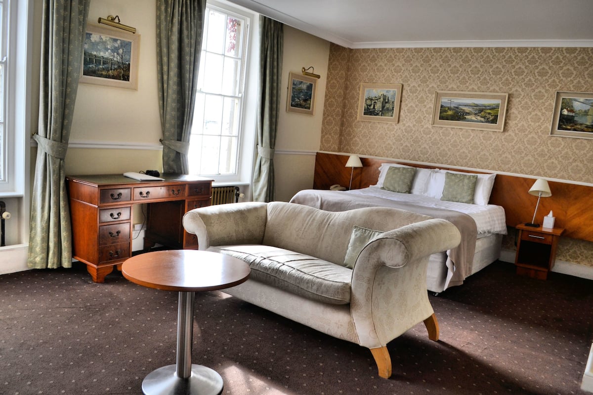 Quarto de hotel com cama, sofá, escrivaninha e mesa redonda.