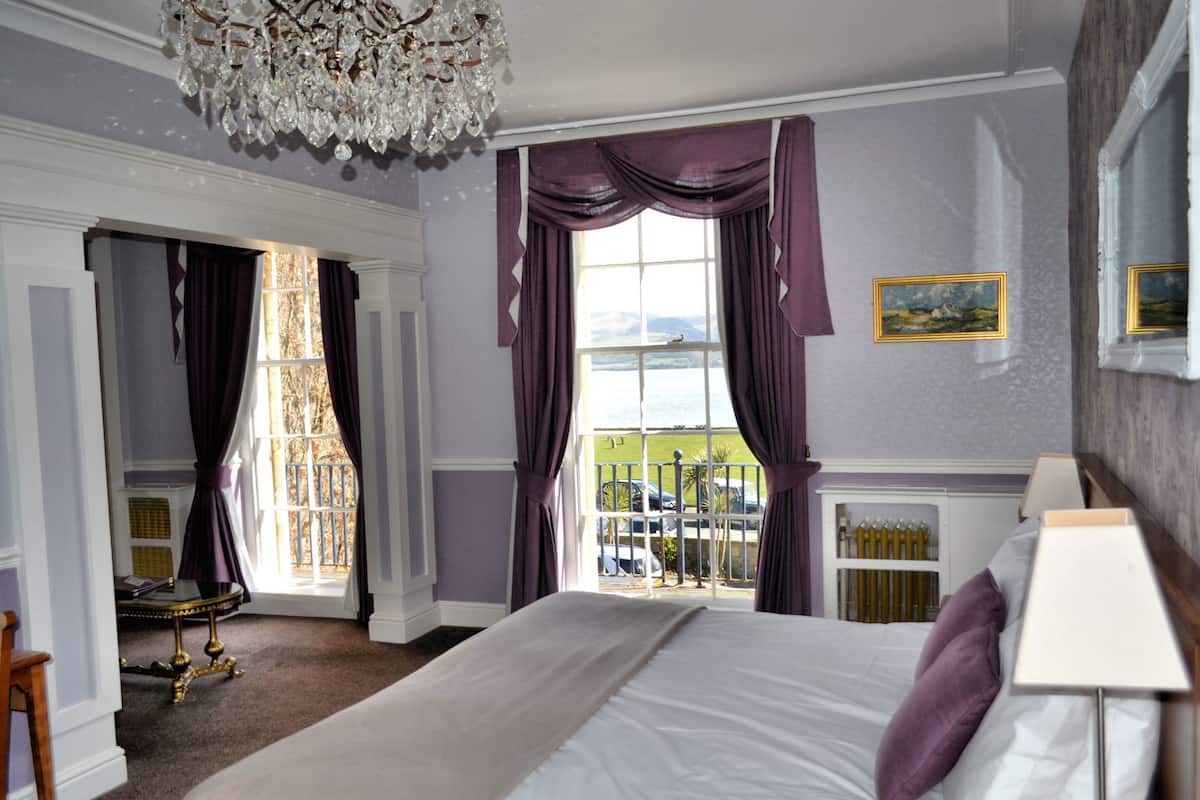 Quarto de hotel com uma cama grande, um candelabro e vista para o exterior.