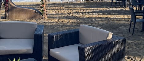 Uma área de estar à beira-mar com móveis de vime e guarda-sóis, com vista para o oceano.