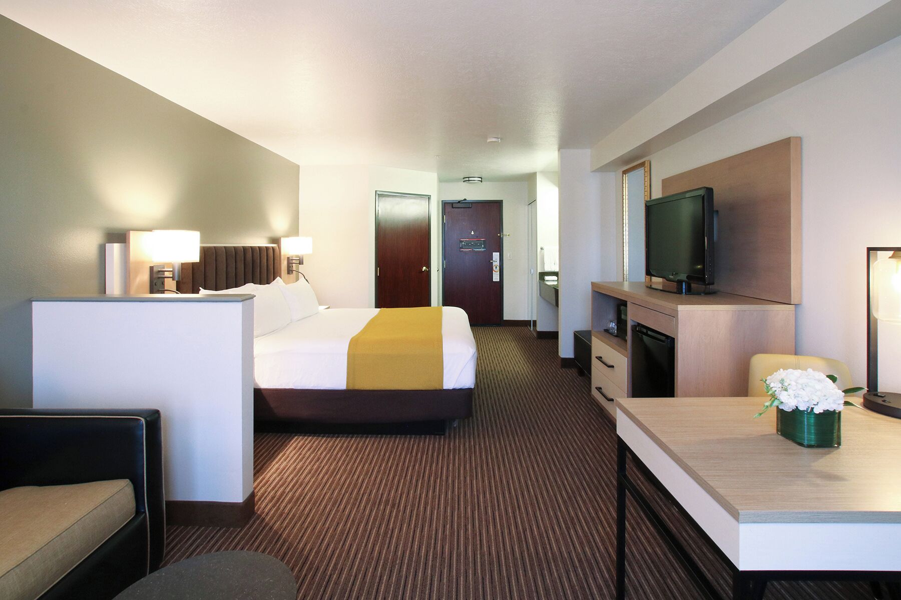 Quarto de hotel com cama, escrivaninha, televisão e porta do banheiro.