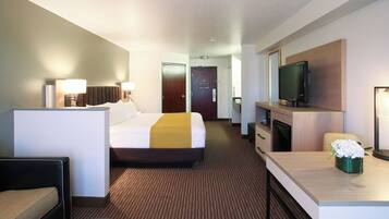 Quarto de hotel com cama, escrivaninha, televisão e porta do banheiro.