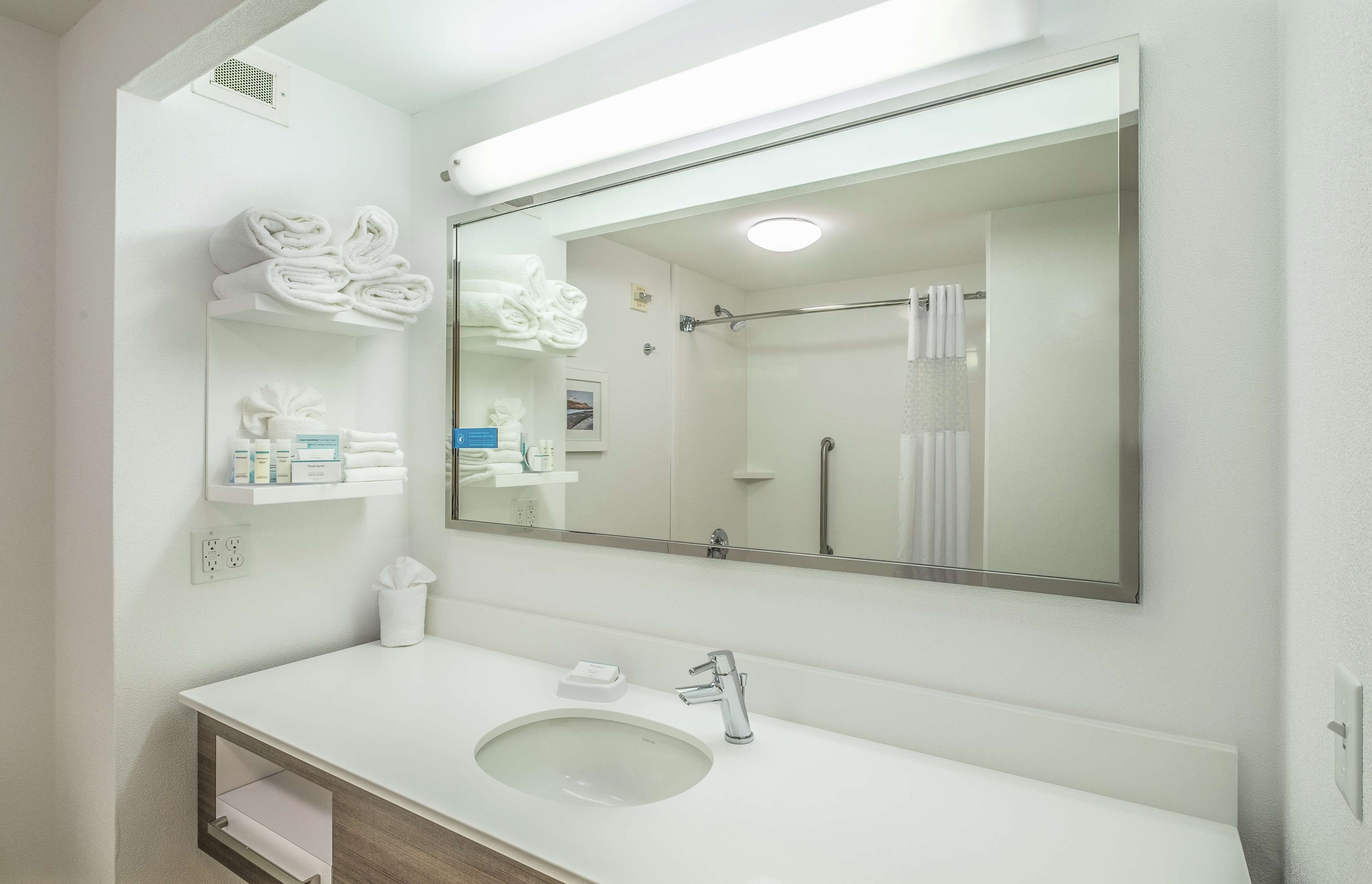 Uma casa de banho moderna com lavatório branco, um espelho grande e toalhas bem dobradas nas prateleiras.