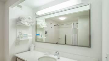 Uma casa de banho moderna com lavatório branco, um espelho grande e toalhas bem dobradas nas prateleiras.