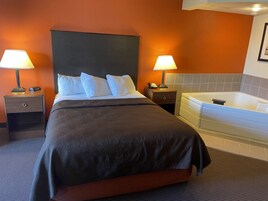 Quarto de hotel com uma cama grande, duas mesas de cabeceira com luminárias, uma banheira integrada e uma moldura com imagem na parede.