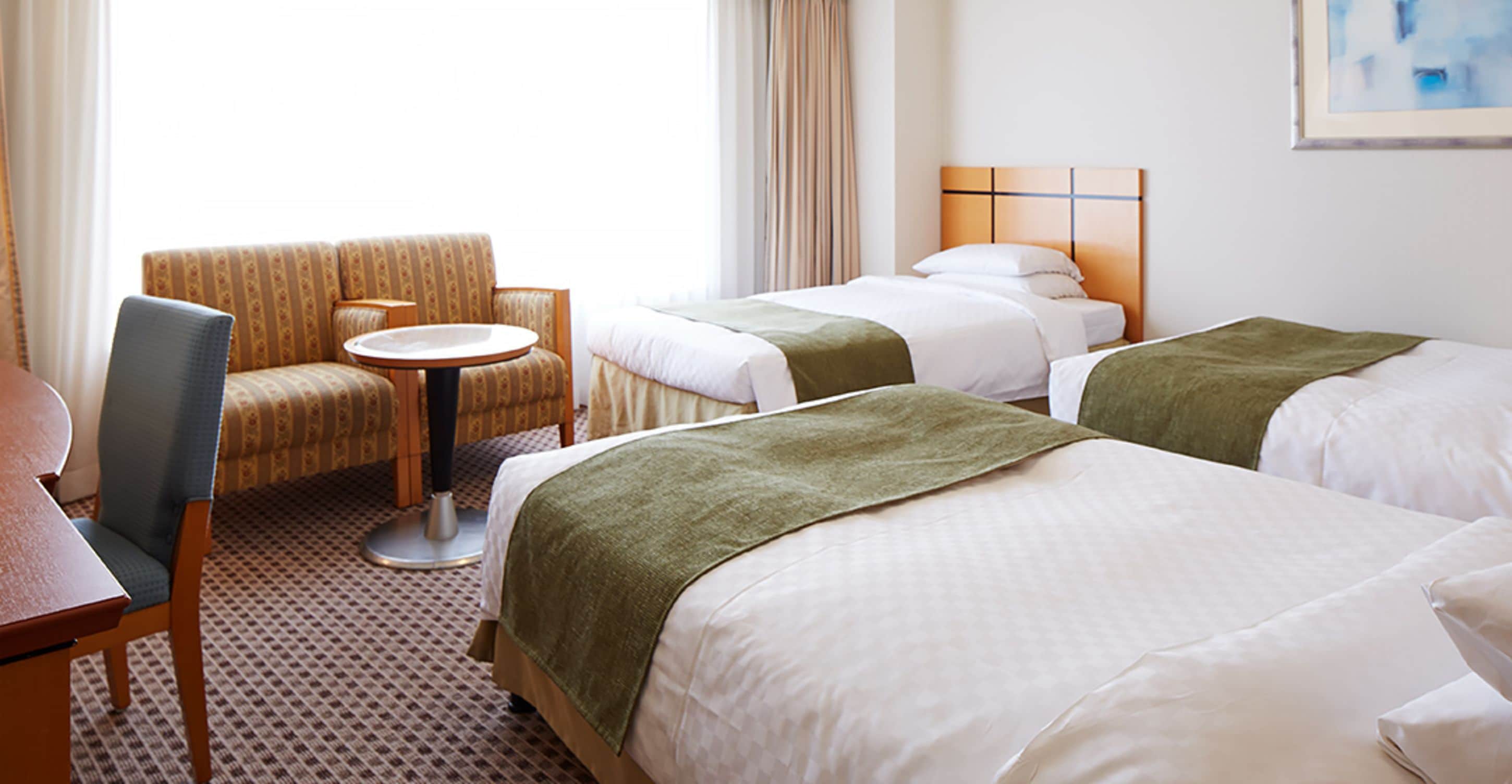 Quarto de hotel com duas camas, um sofá, uma mesinha e uma cadeira.