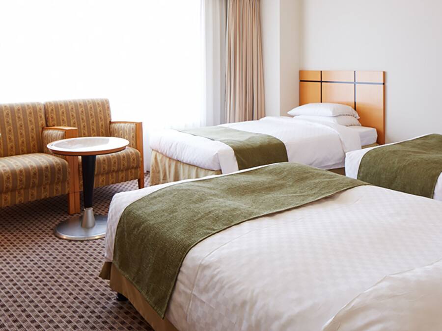 Quarto de hotel com duas camas, um sofá, uma mesinha e uma cadeira.