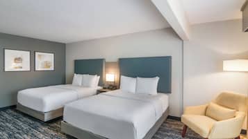 Quarto de hotel com duas camas, uma cadeira e obras de arte na parede.