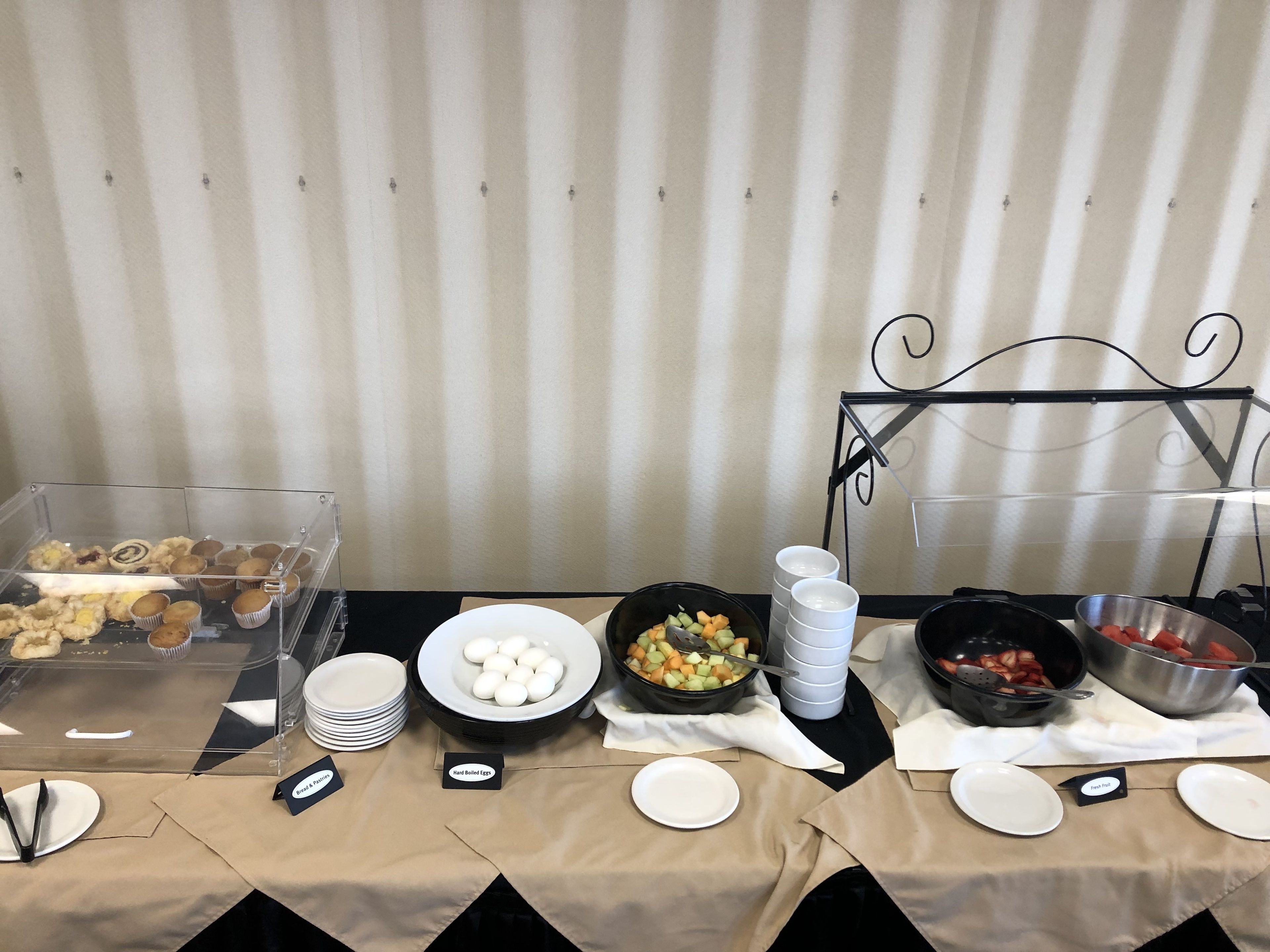 Uma mesa de buffet com diversos alimentos, incluindo ovos cozidos, frutas e um recipiente com doces.