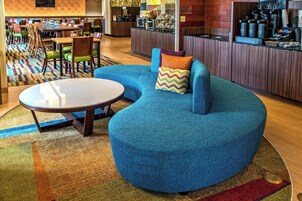 Espaço lounge moderno com um sofá azul, uma mesa redonda e um tapete colorido.