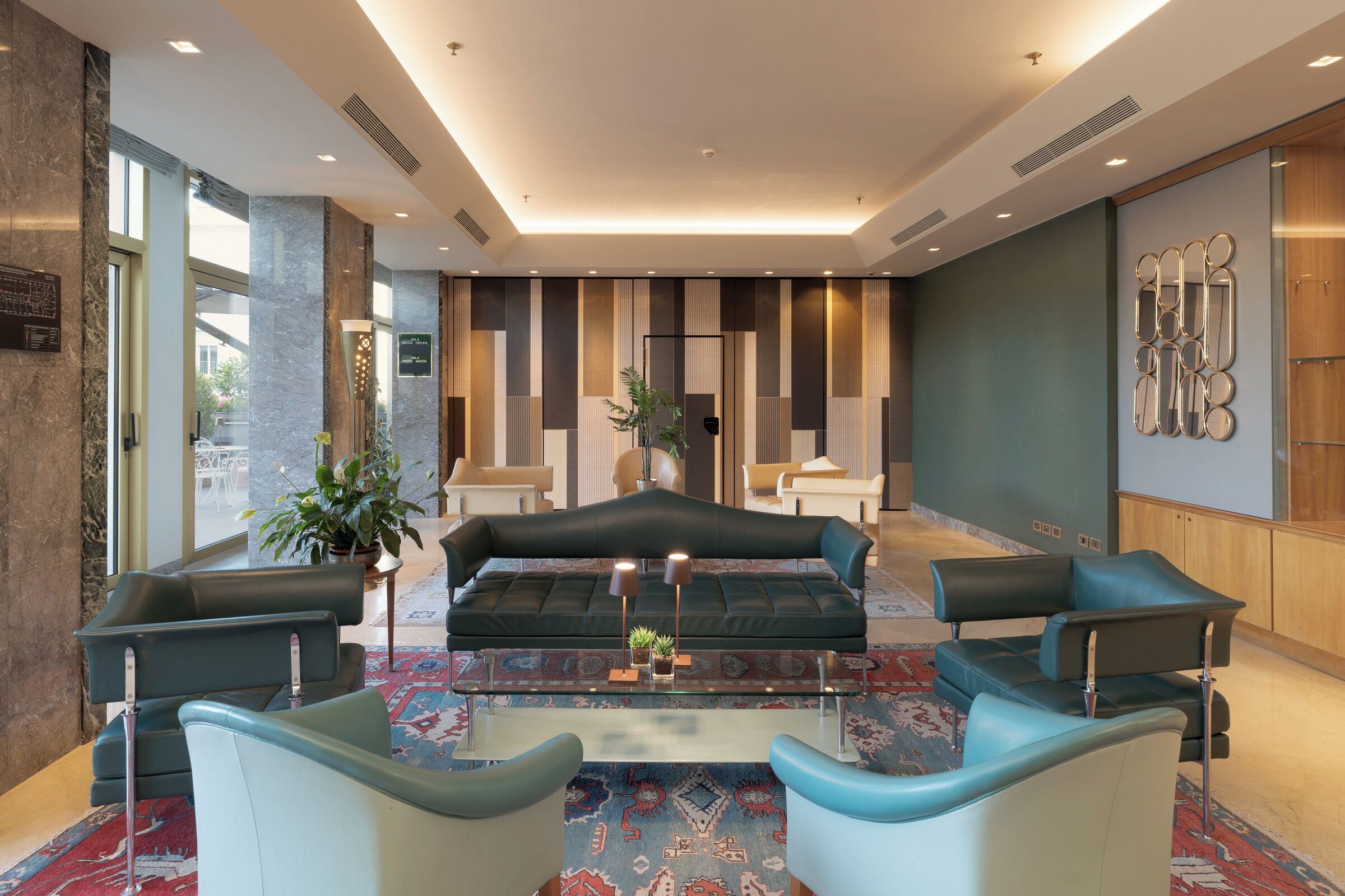 Um hall com sofá, cadeiras, mesa de centro e um espelho decorativo.