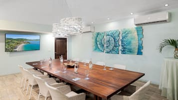 Uma sala de conferências com uma mesa de madeira comprida, cadeiras de vime, uma grande tela de televisão e arte abstrata nas paredes.