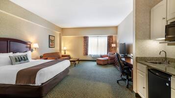 Quarto de hotel com uma cama grande, uma escrivaninha, uma cadeira, uma televisão, um micro-ondas e uma pia.
