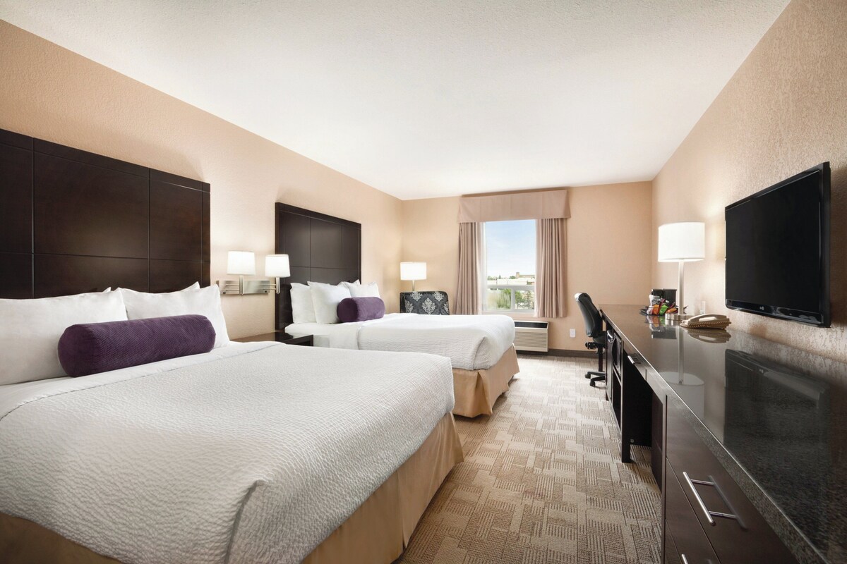 Quarto de hotel com duas camas, uma escrivaninha, uma televisão e uma janela com vista.