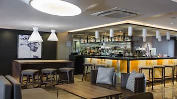 Uma área de bar com banquetas, um balcão com garrafas e um espaço de estar com mesas e cadeiras.