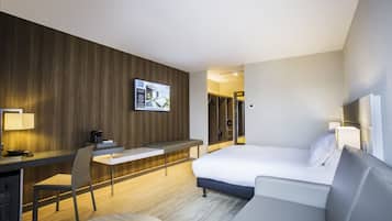 Quarto de hotel moderno com cama, escrivaninha, cadeira e televisão fixada na parede.