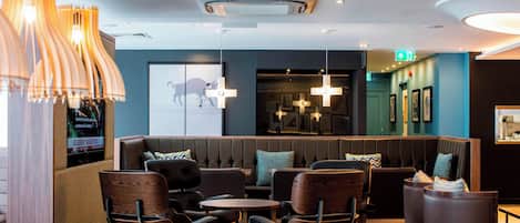 Restaurante moderno com área de assentos em cabines, cadeiras de madeira e iluminação pendente.